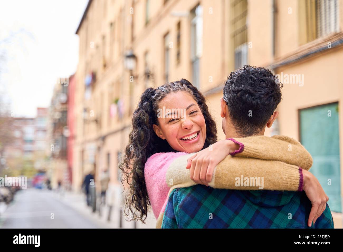 Young latin woman hugs her boyfriend from behind and smiles at him ...
