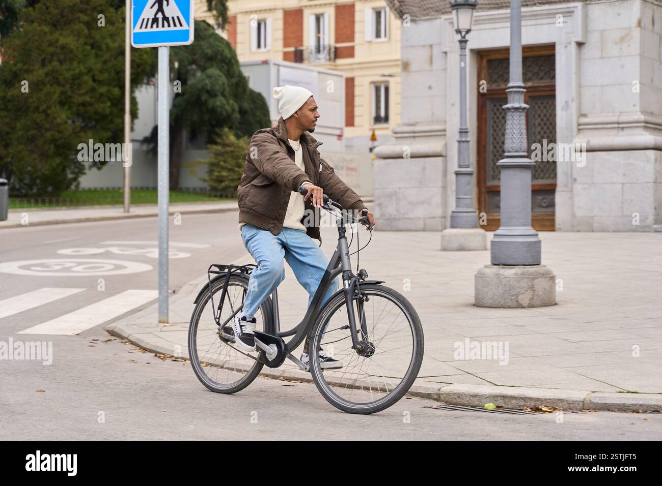 Stylish man cycling in the city on a gray bicycle next to a crosswalk ...