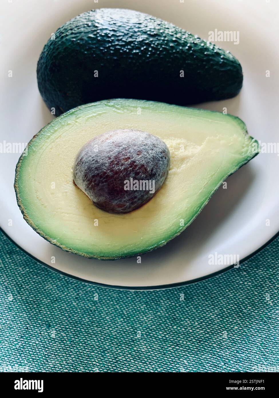 Avocado split in half in a plate isolated on a green background ...