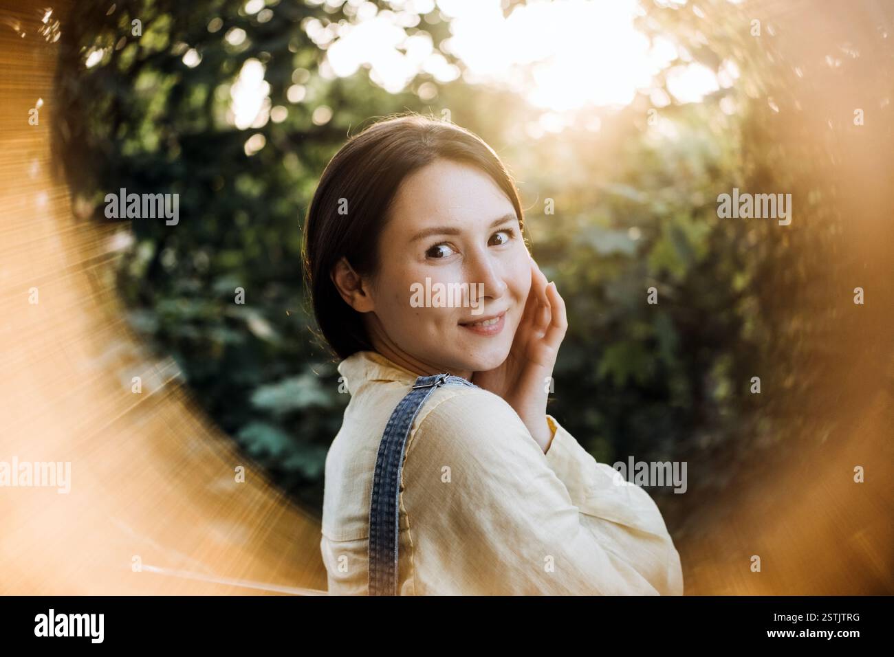 Smiling woman looking back with sunlight and forest backdrop. Joy ...