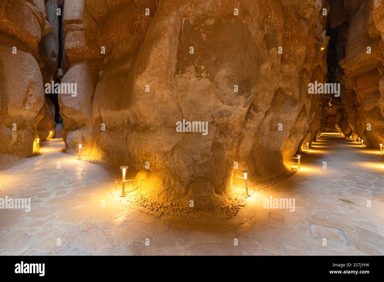 Warm toned lights illuminate a paved path winding through towering rock ...