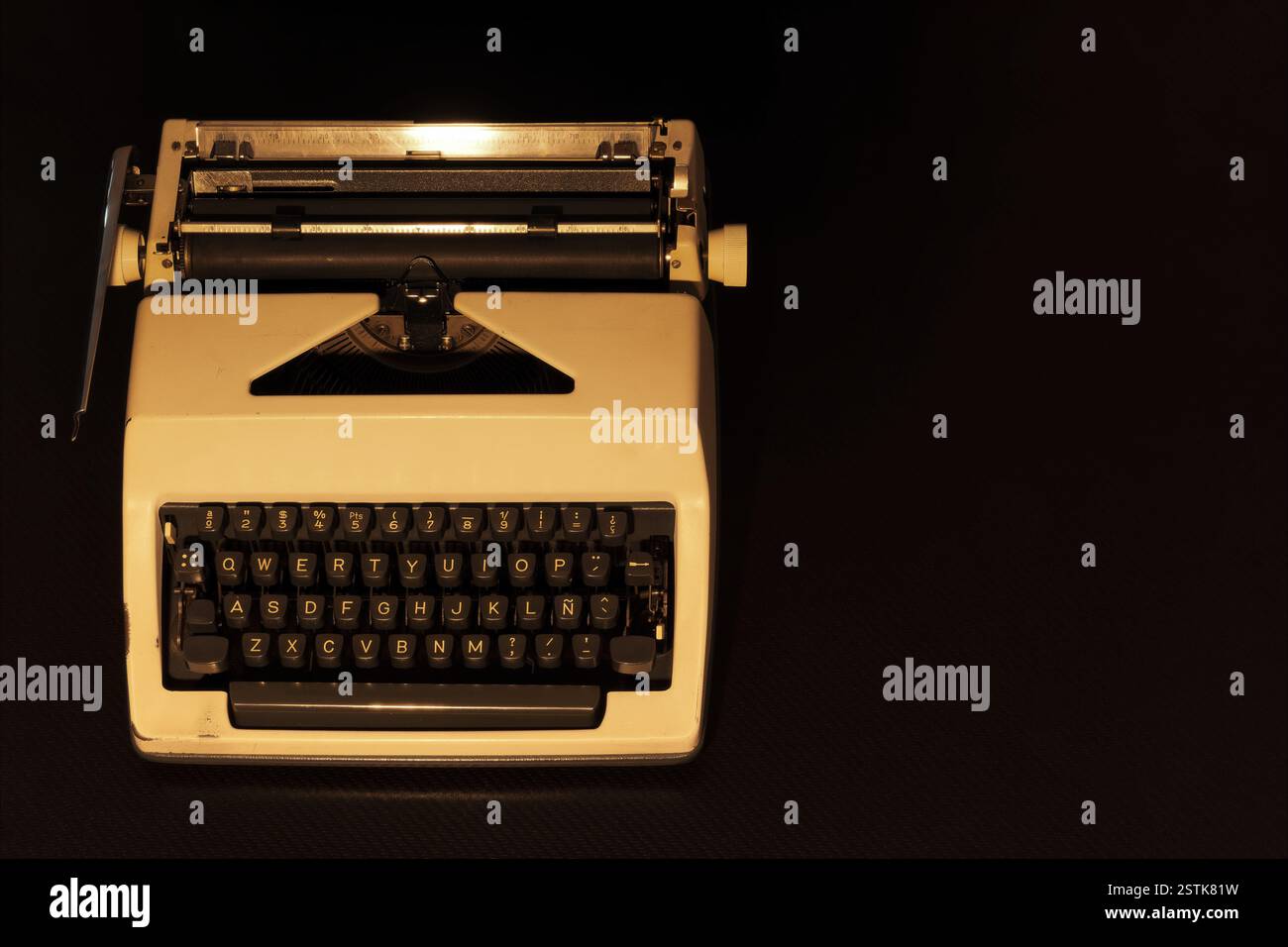 A vintage beige typewriter on a moody dark background. The machine's ...