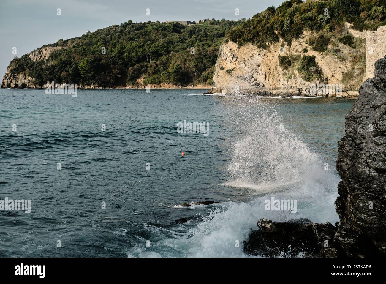 Dramatic coastal scene where a wave crashes against jagged rocks. The ...