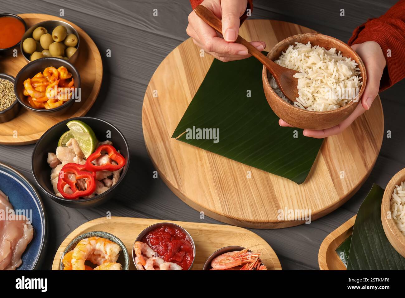 Woman putting rice onto banana leaf at wooden table with products ...