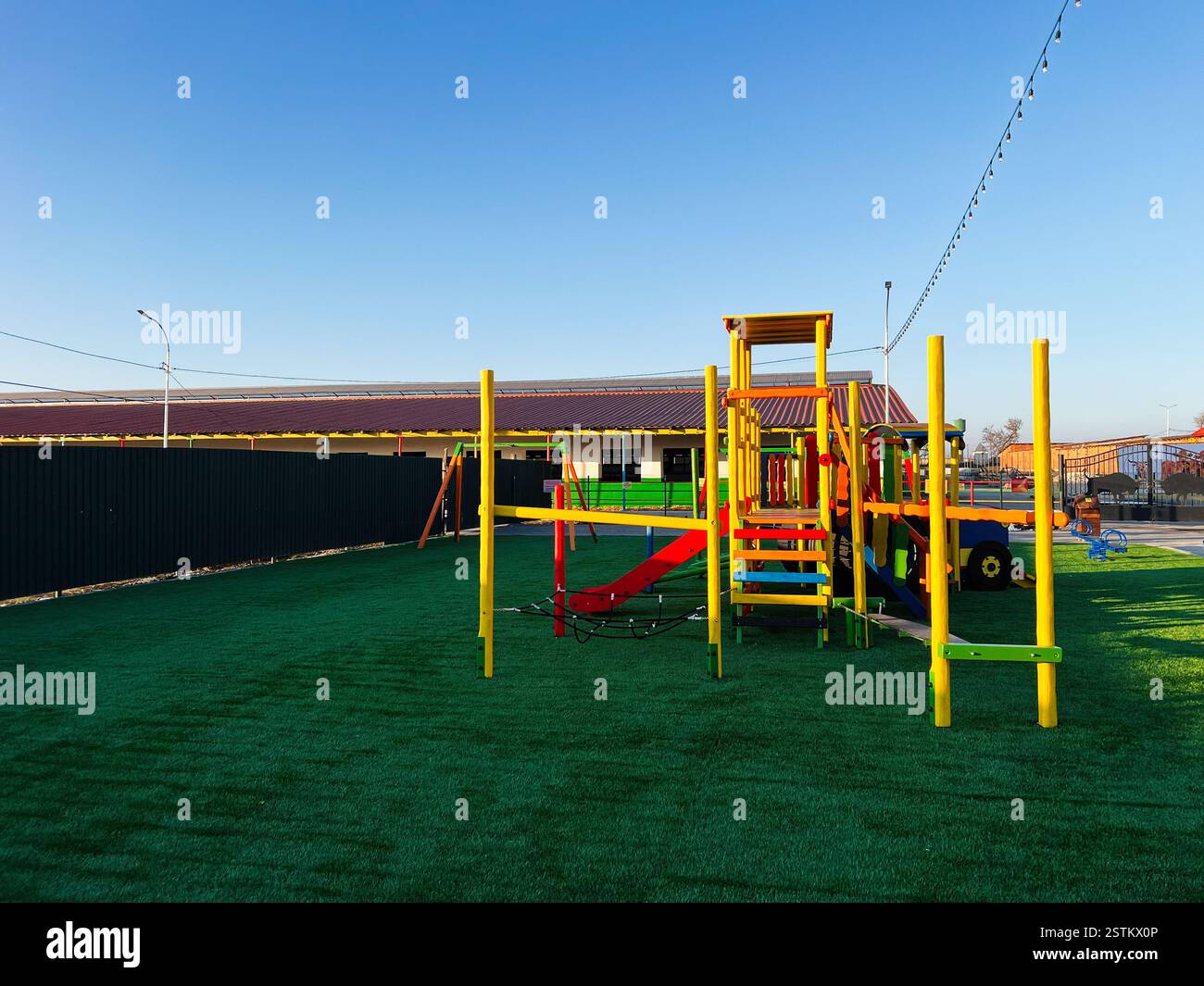 Vibrant wooden play structures on green grass surrounded by fencing ...
