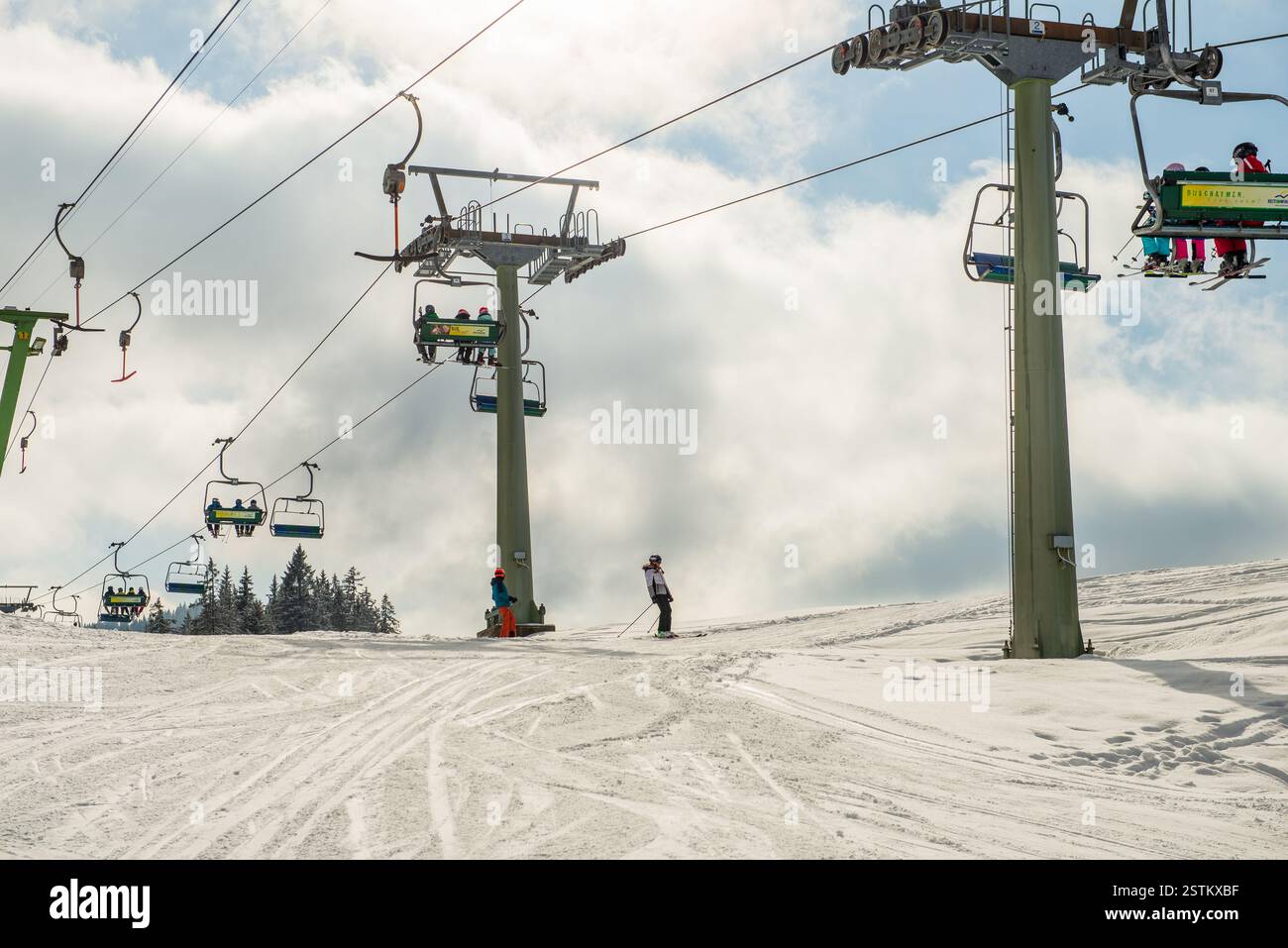 Skiers ride on a chair lift up a slope while others ski beneath it ...