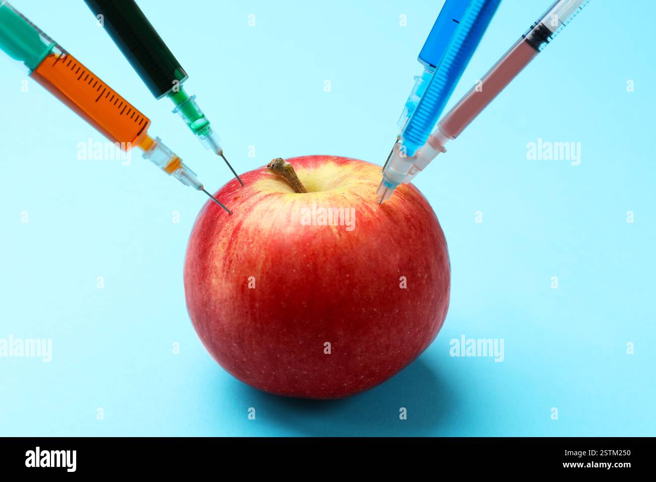 GMO concept. Red apple with different syringes on light blue background ...