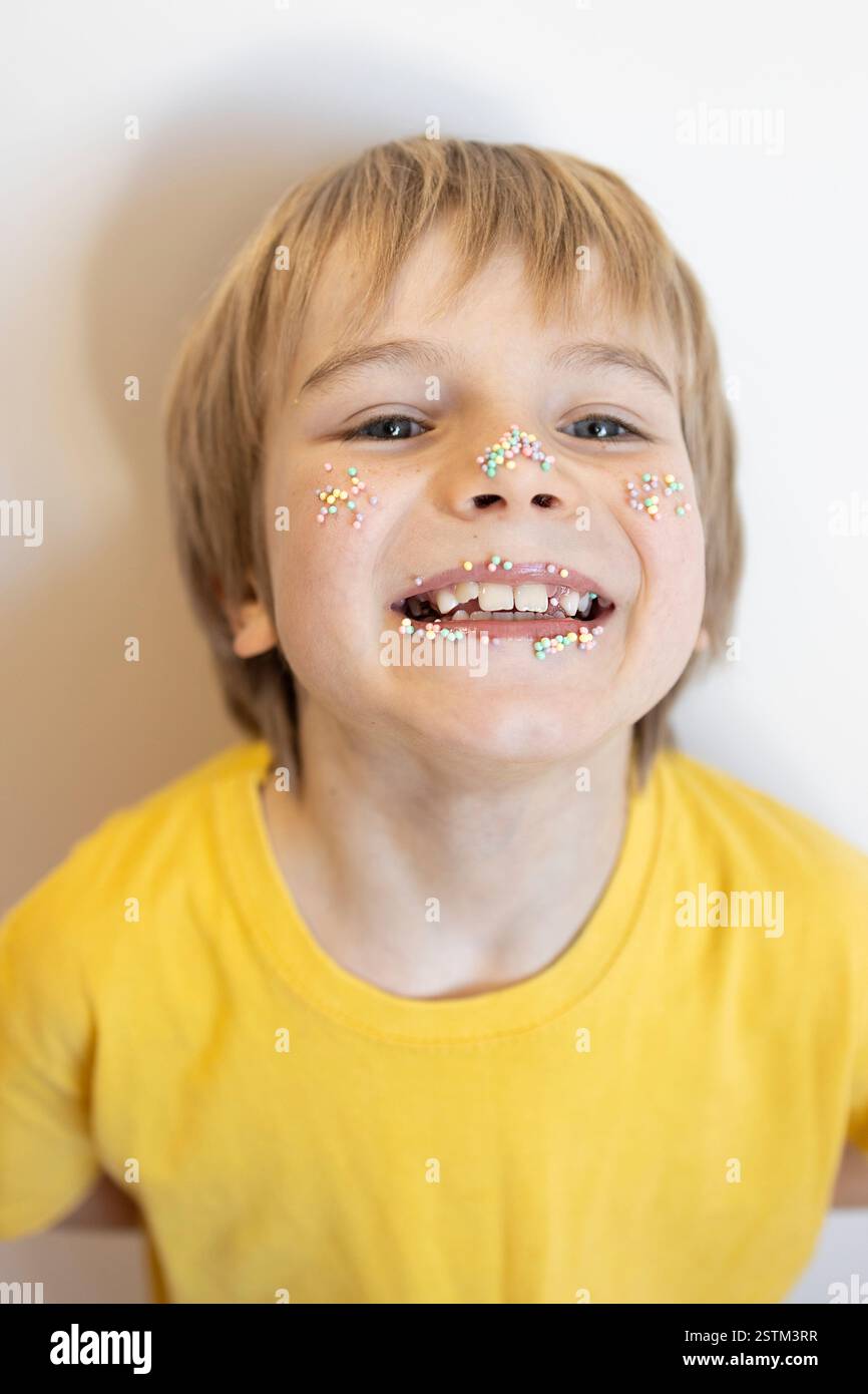 Funny boy portrait with small colorful sugar sprinkles stuck to face ...