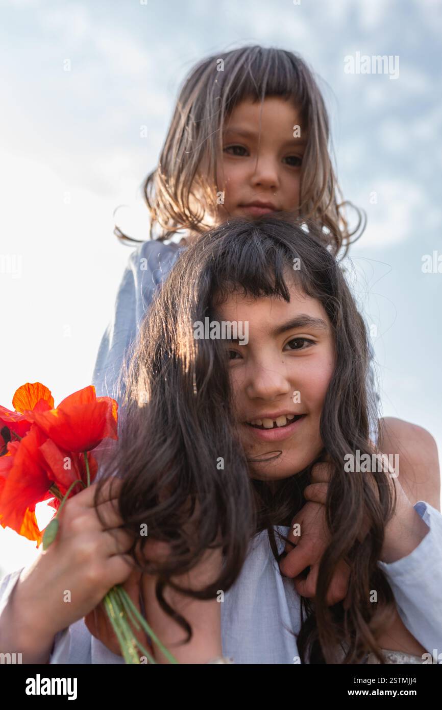 portrait of two children, smaller kid sitting on elder sister against ...