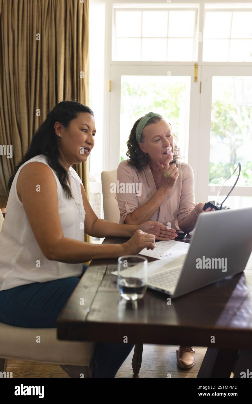 Senior women collaborating on laptop at home, discussing project with ...