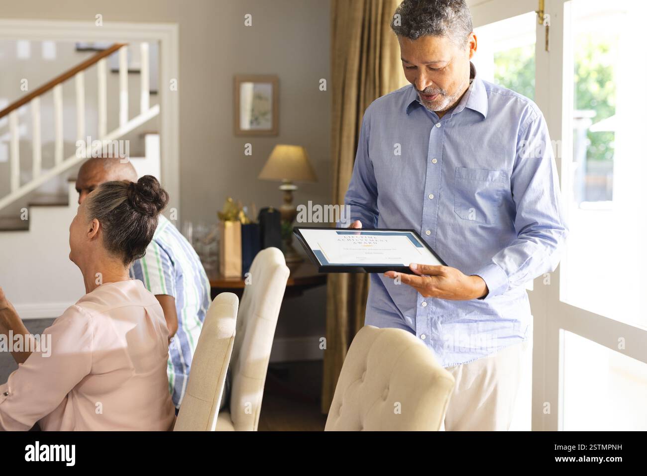 Senior man proudly holding award certificate at family gathering in ...