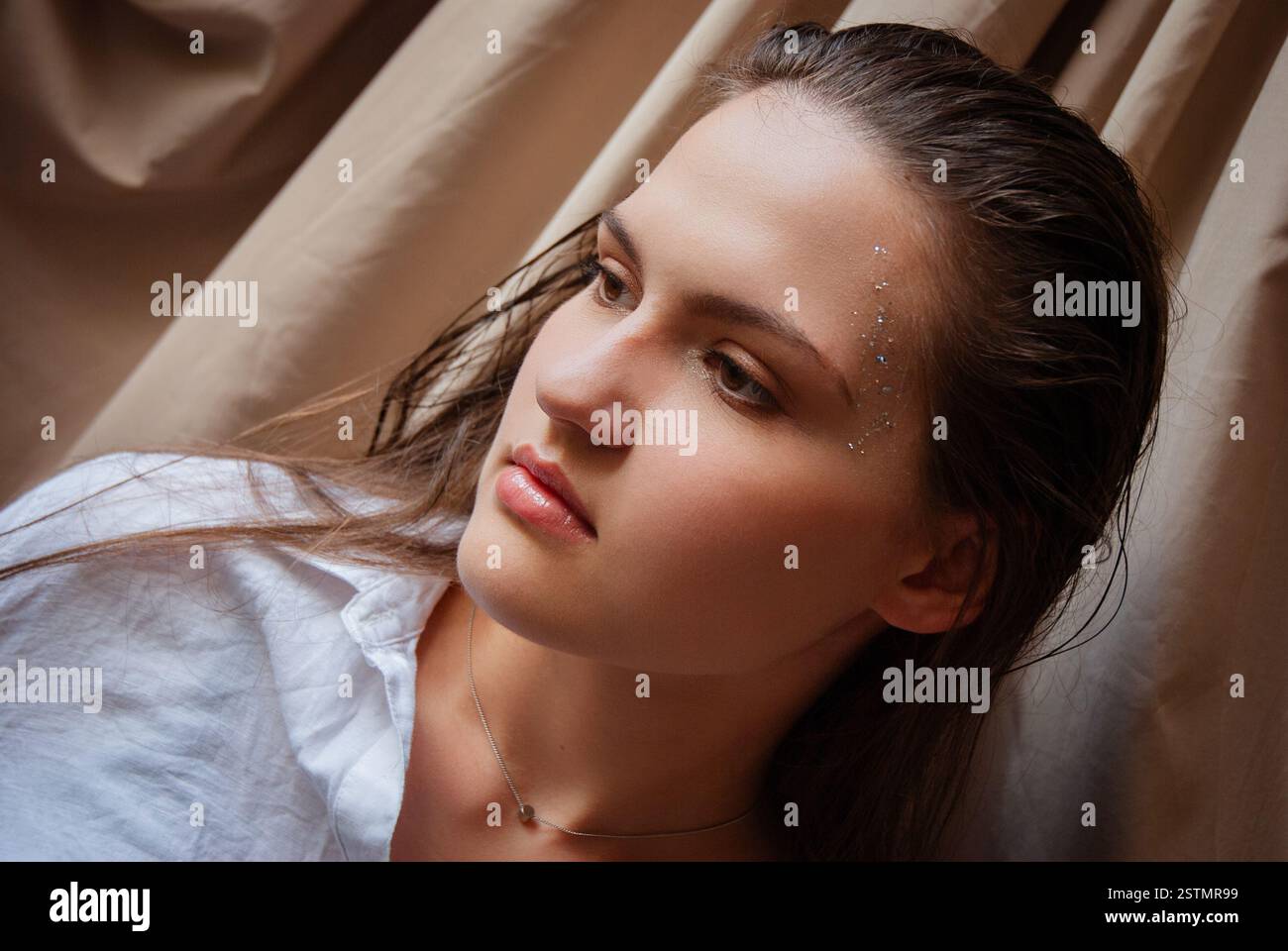 Contemplative portrait with subtle makeup and wet hair on neutral ...