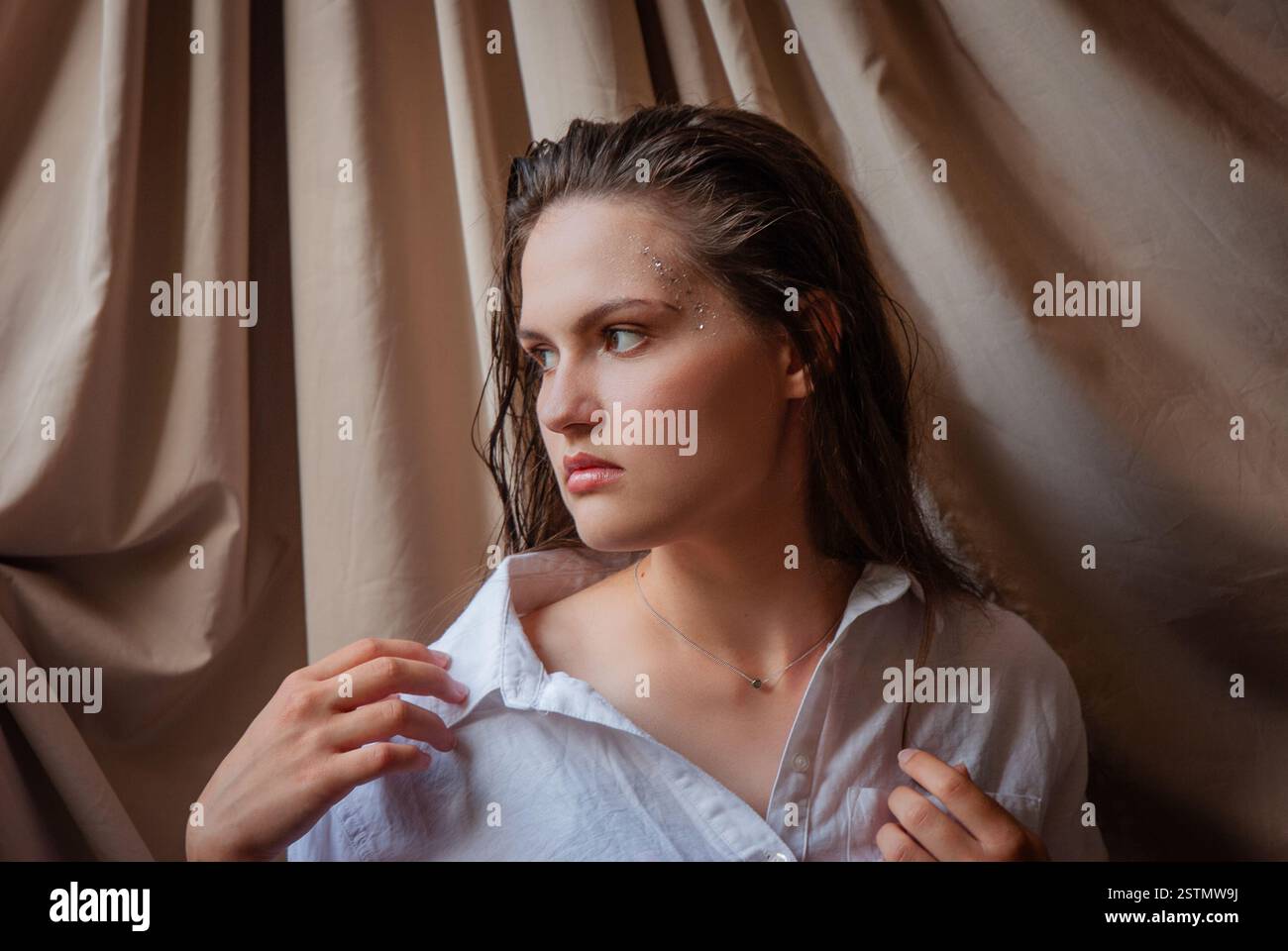 Contemplative young woman in white shirt with dramatic draped fabric ...