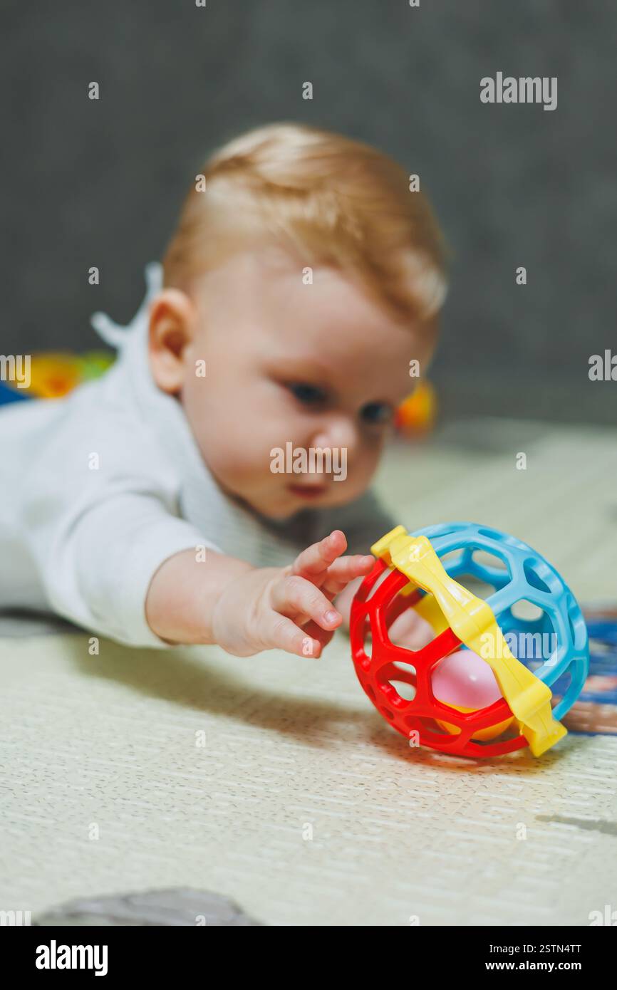 A baby reaching for a colorful toy ball, showing curiosity and ...