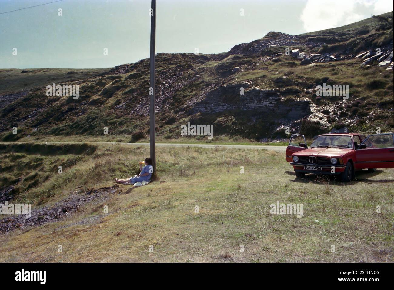 Girl Sitting Against A Telegraph Pole Adjacent To A Red Bmw 320 Car In