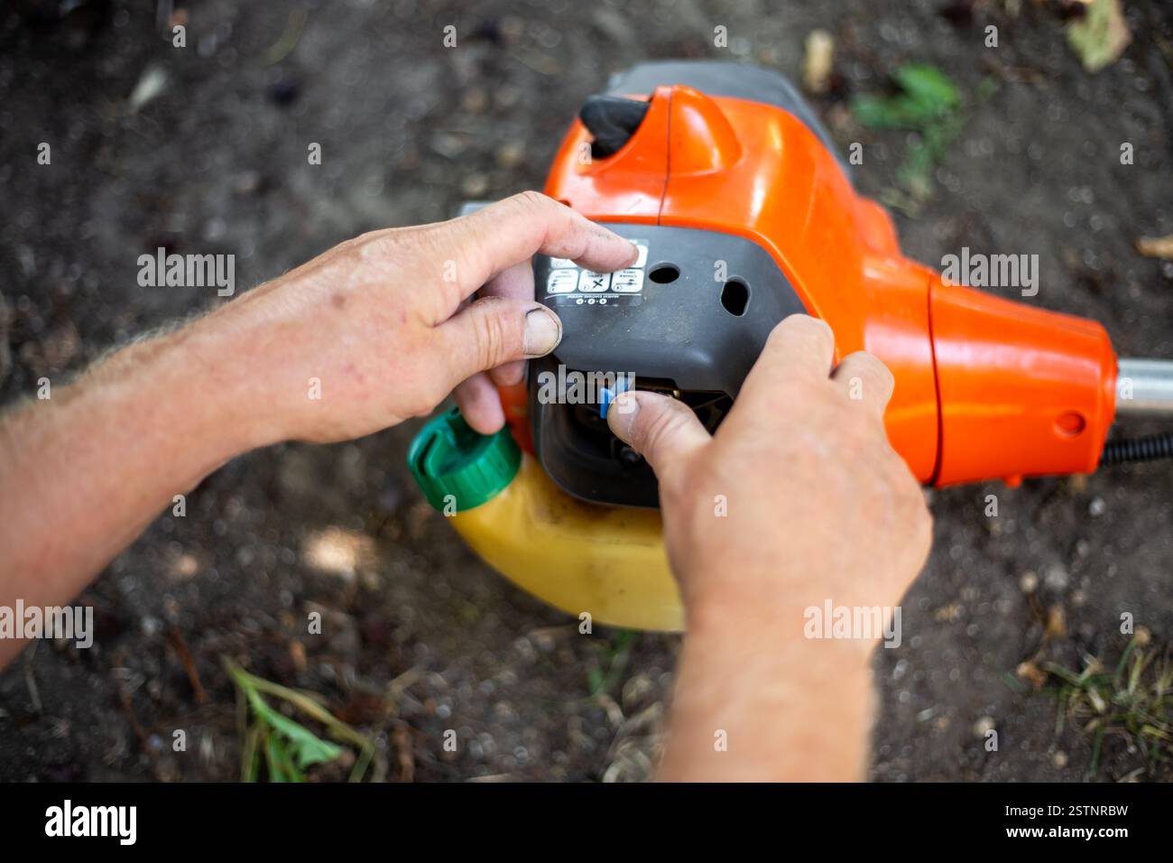 Starting a gas trimmer to mow the grass. A man opens the choke to make ...