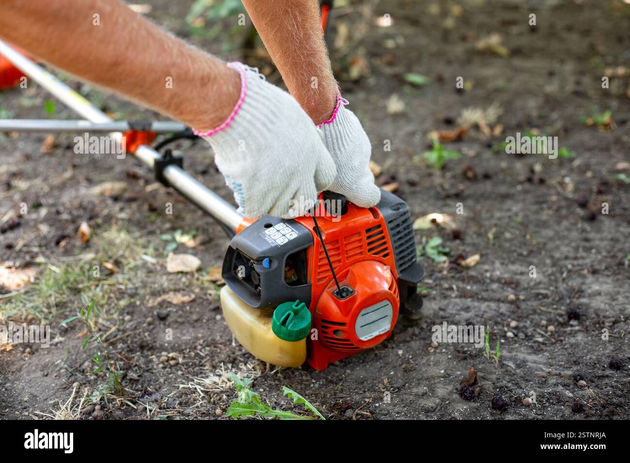 Starting a gas mower to cut grass. A man pulls the recoil starter to ...