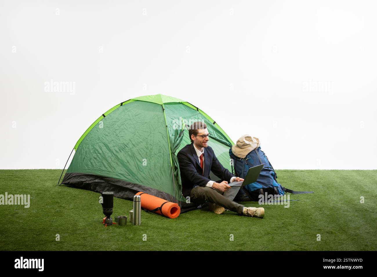 Businessman sitting near camping tent working on laptop, smiling ...