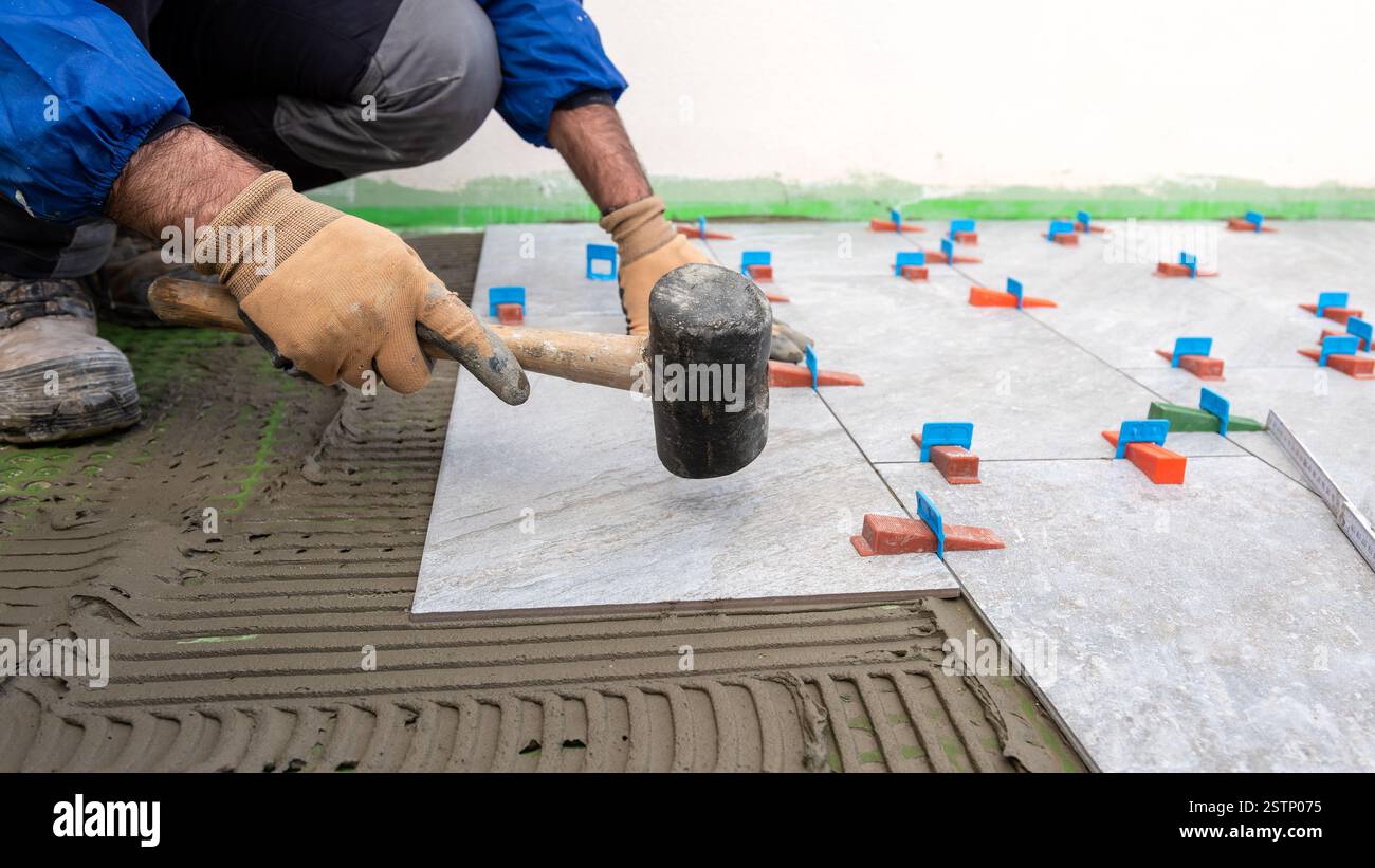 Bricklayer tiler with black rubber hammer puts in place tiles for a new ...