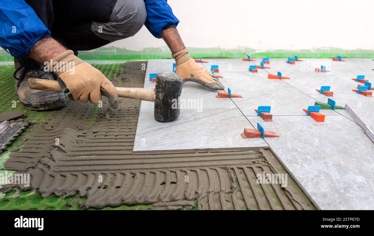 Bricklayer tiler with black rubber hammer puts in place tiles for a new ...