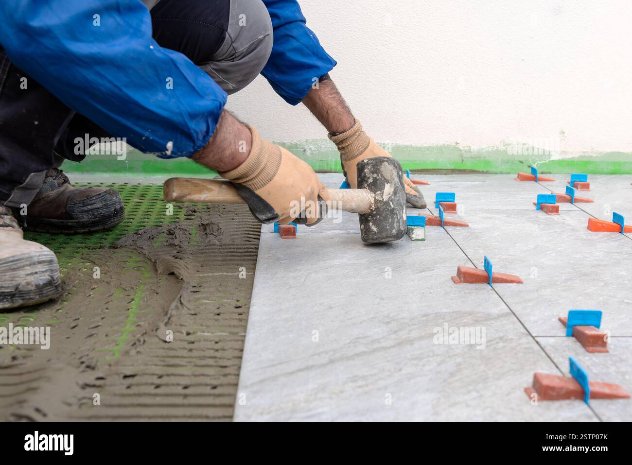 Bricklayer tiler with black rubber hammer puts in place tiles for a new ...