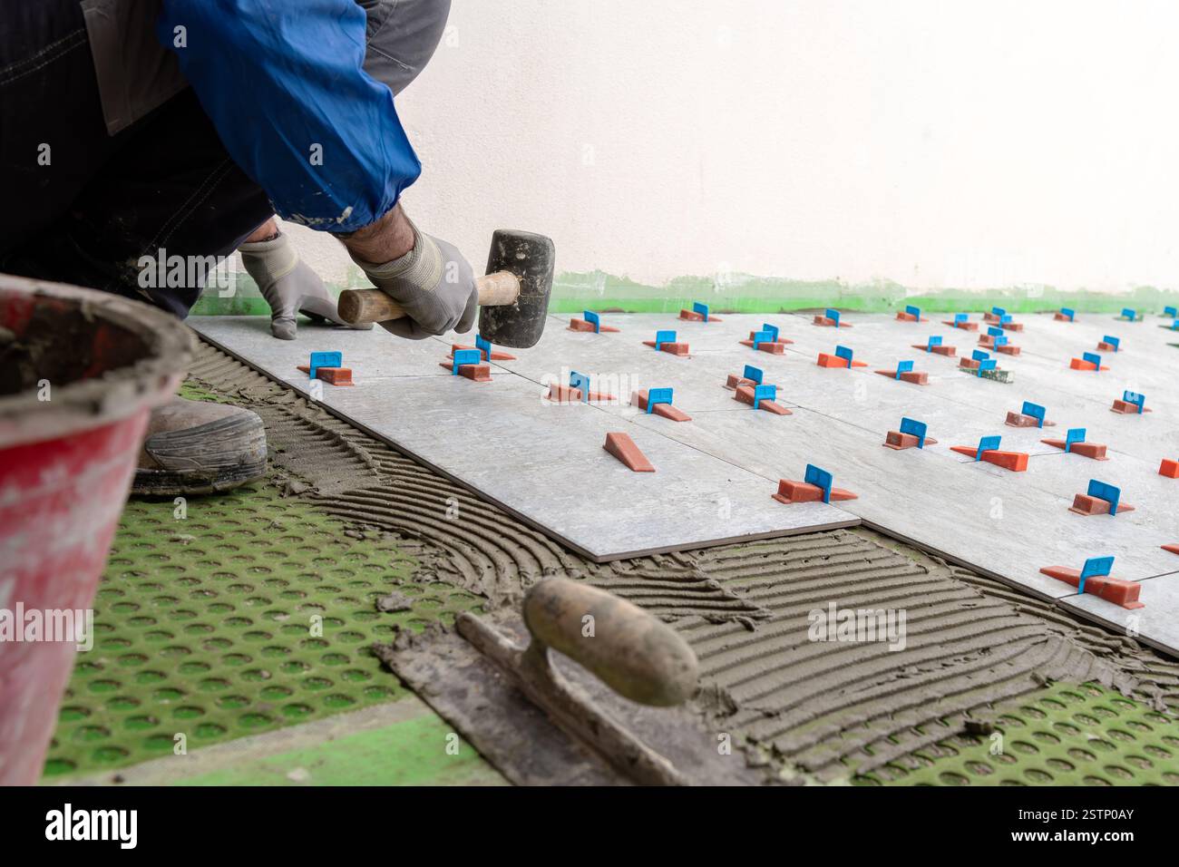 Bricklayer tiler with black rubber hammer puts in place tiles for a new ...