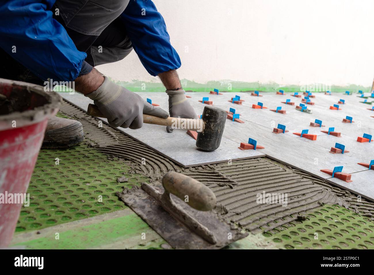 Bricklayer tiler with black rubber hammer puts in place tiles for a new ...