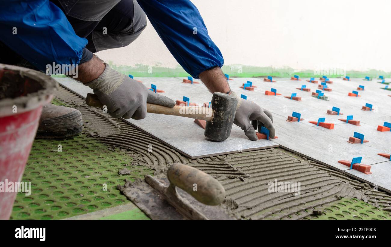 Bricklayer tiler with black rubber hammer puts in place tiles for a new ...