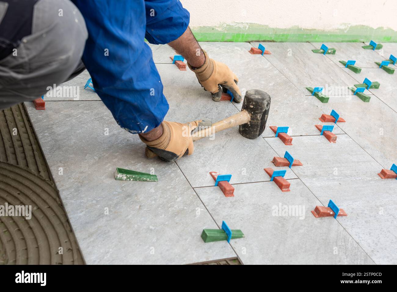 Bricklayer tiler with black rubber hammer puts in place tiles for a new ...