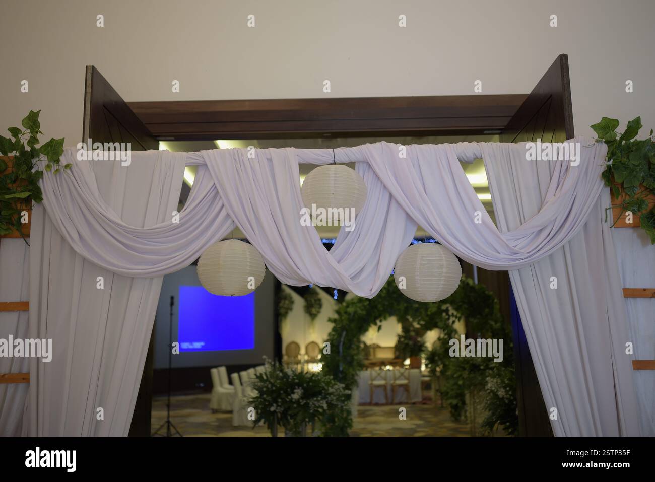 An aesthetically designed event entrance. White draped fabric cascades ...