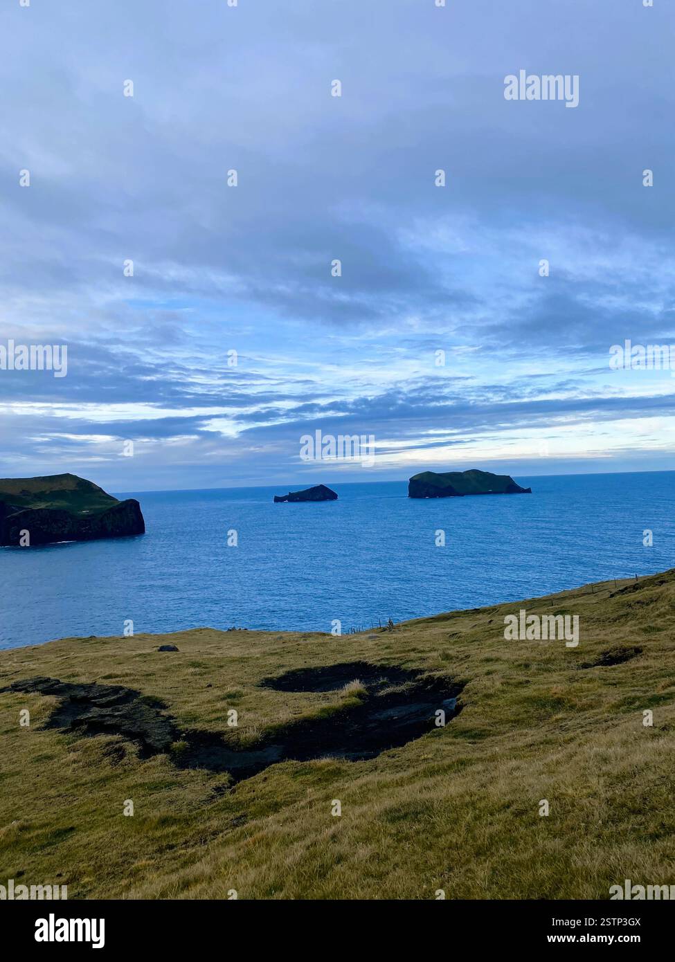 A coastal landscape featuring grassy hills, calm sea, and distant ...