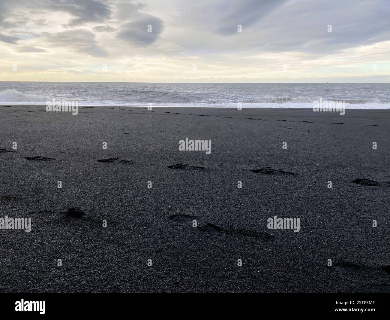 The image depicts a serene beach scene with unique black sand, gentle ...