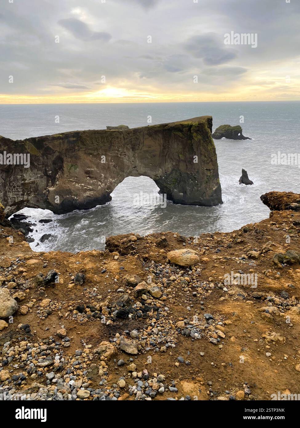 A rugged coastal landscape featuring a natural rock arch, with uneven ...