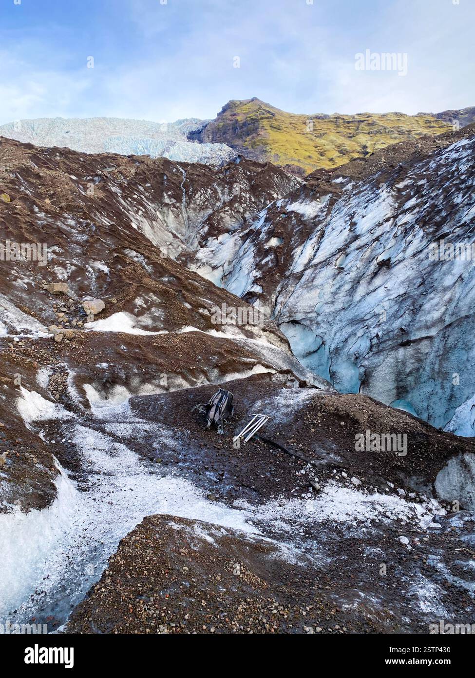 A rugged glacial landscape with dark soil, blue ice formations, and ...