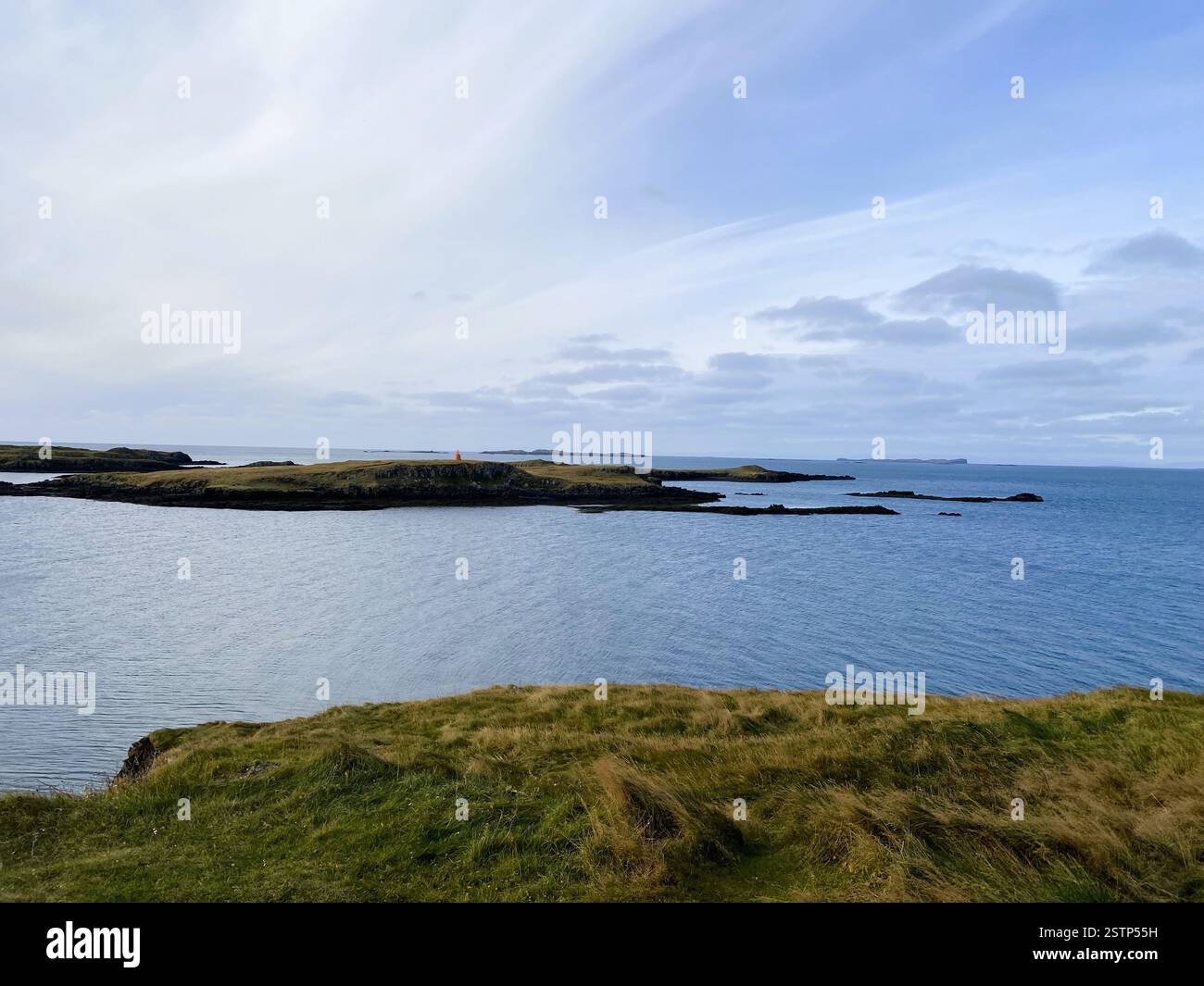 A serene coastal landscape with calm sea, grassy slopes, and distant ...