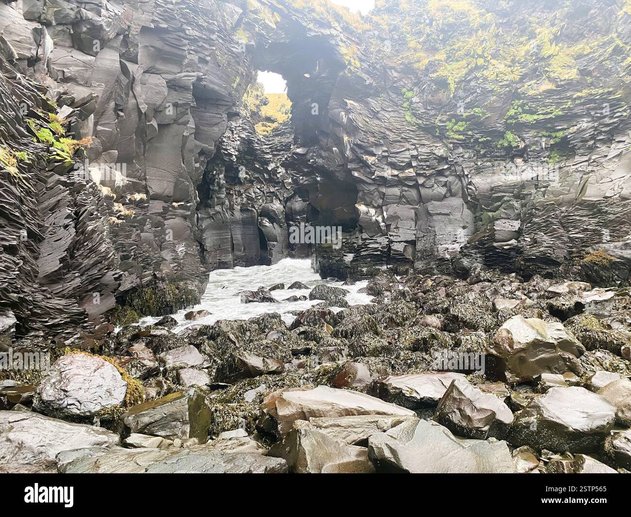 A rugged coastal scene with dark stones, towering cliffs, and a natural ...
