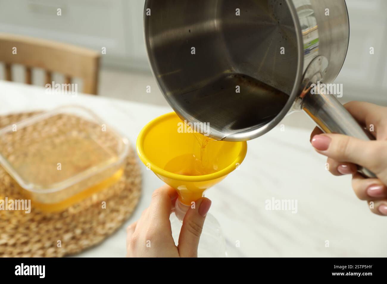 Woman pouring used cooking oil into bottle through funnel in kitchen ...