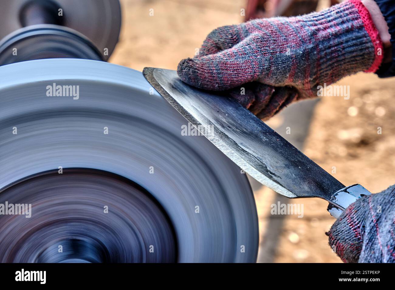 A tool being sharpened on a rotating grinding stone, with gloved hands ...