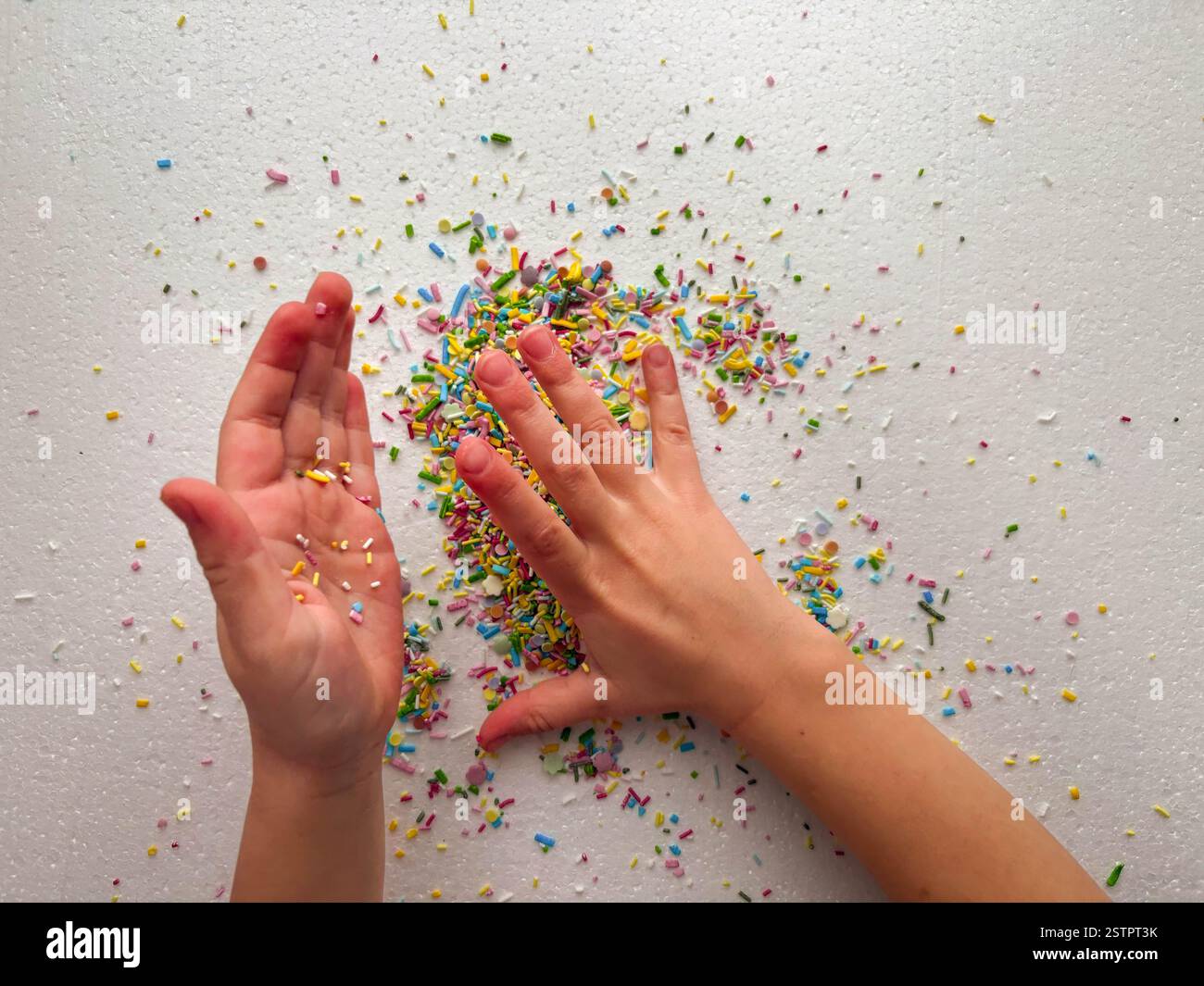 Child playing with colored sugar candies on white background ...