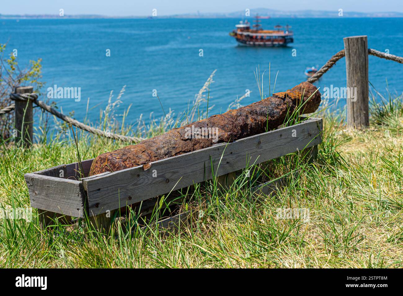 Rusty old cannon on the seashore. In the background a sailing ship ...