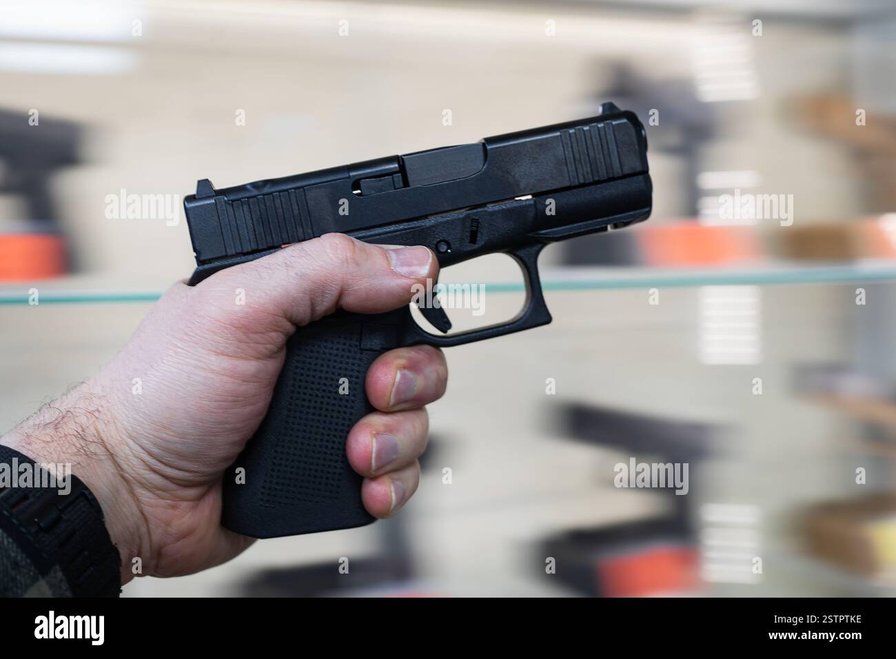 Modern compact 9mm pistol in a man's hand in a gun shop, soft focus ...