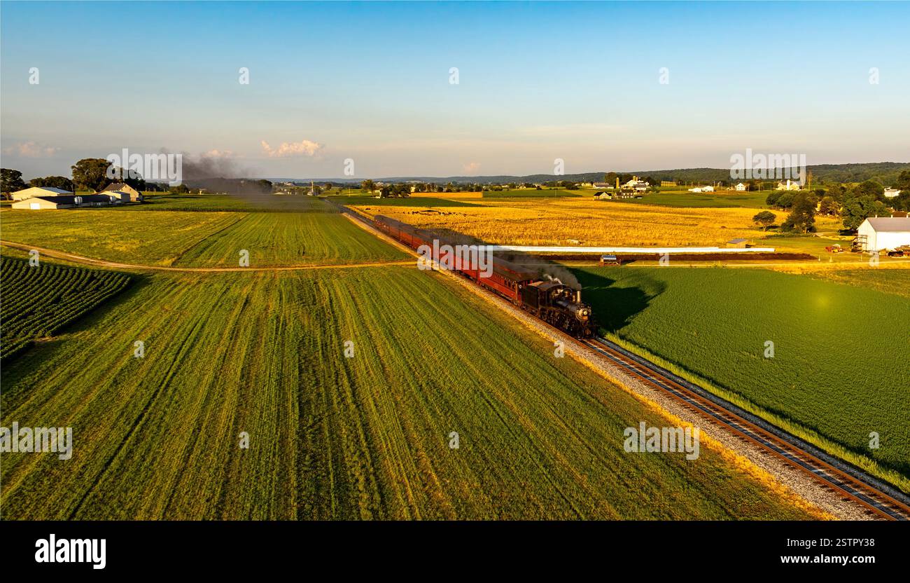 A steam train chugs along the tracks, billowing smoke into the evening ...