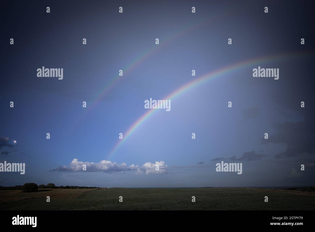 A mesmerizing double rainbow stretches across the sky over open fields ...