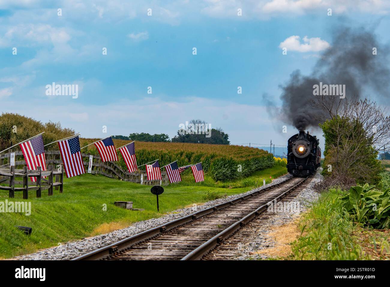 A steam locomotive puffs black smoke as it approaches a rural area ...