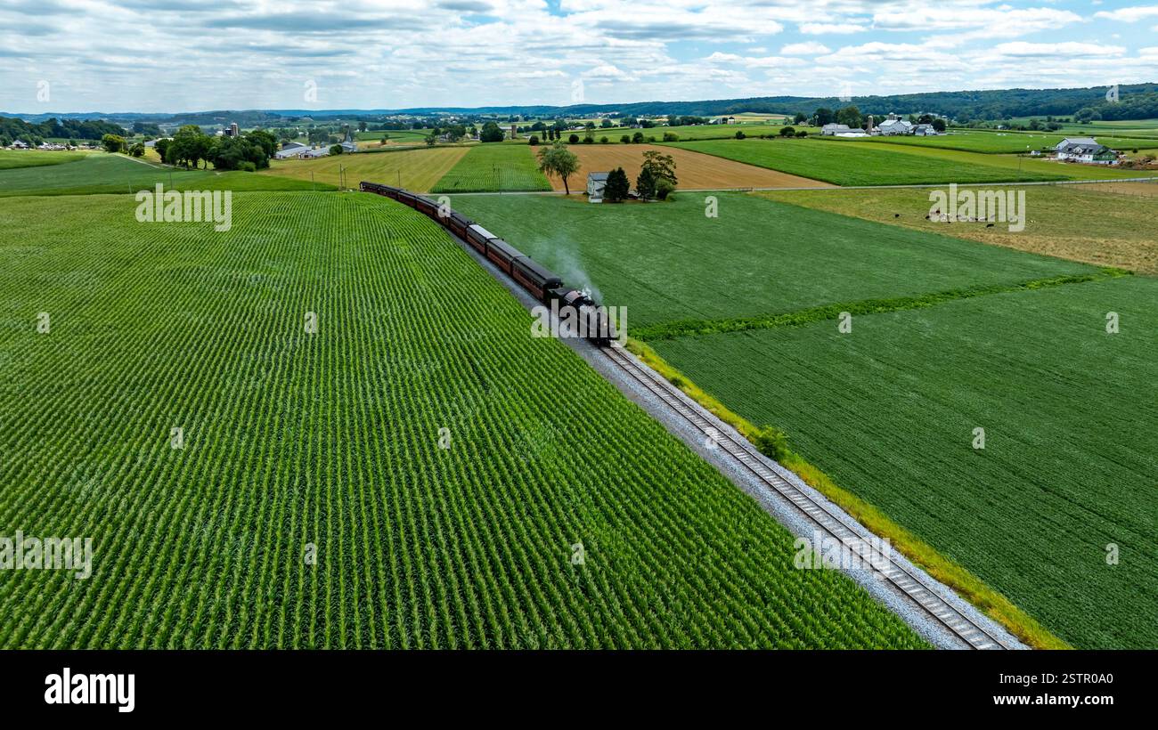 A vintage train moves through lush green fields, surrounded by farmland ...