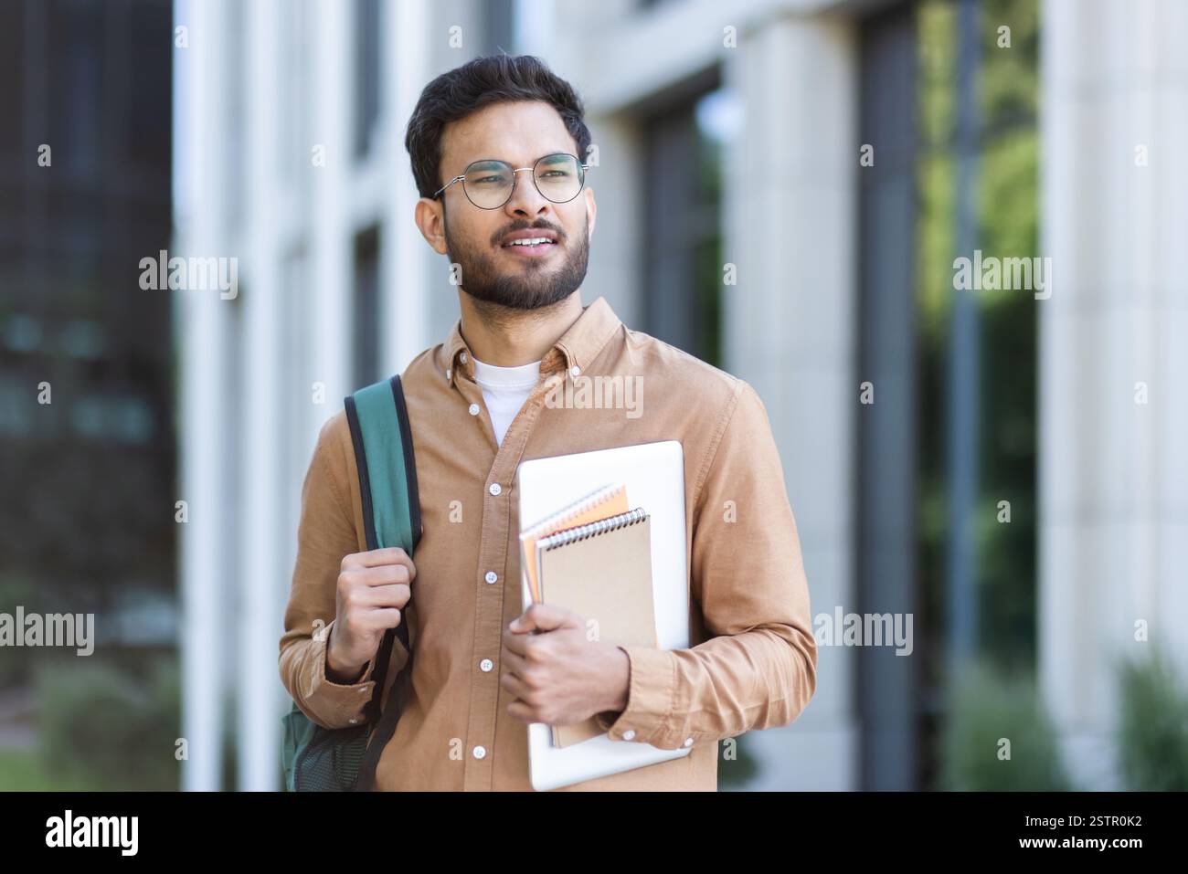Student walking outside university campus with books in hand. Young man ...