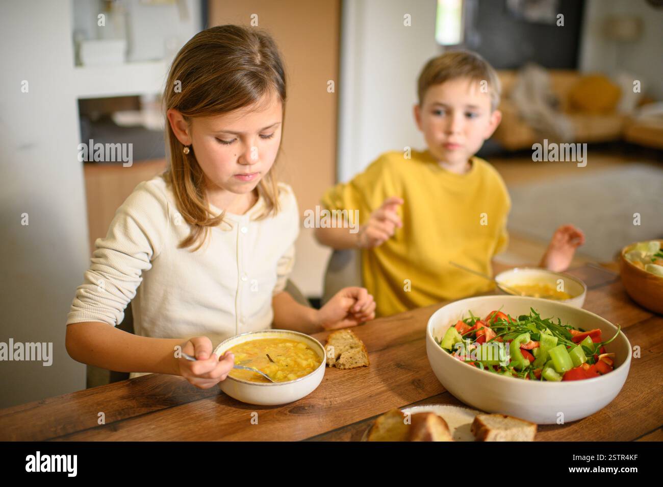 children sit at the table with a plates in front of them. A large bowl ...