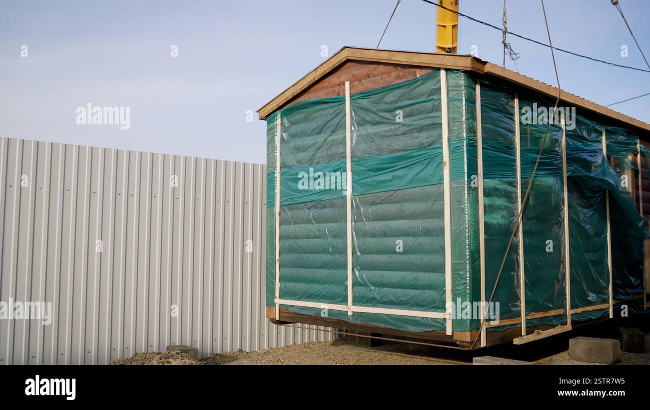 Crane lifting prefabricated wooden house module covered with protective ...