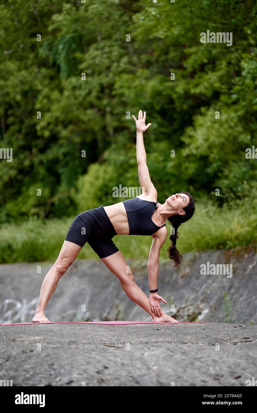 Woman performing extended triangle pose outdoors on yoga mat ...
