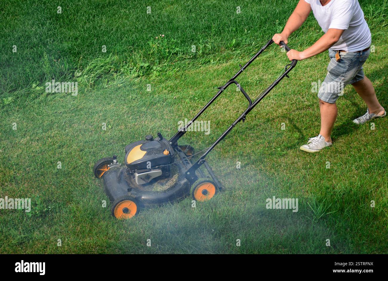High angle view of a man mowing green grass with gas powered lawn mower ...